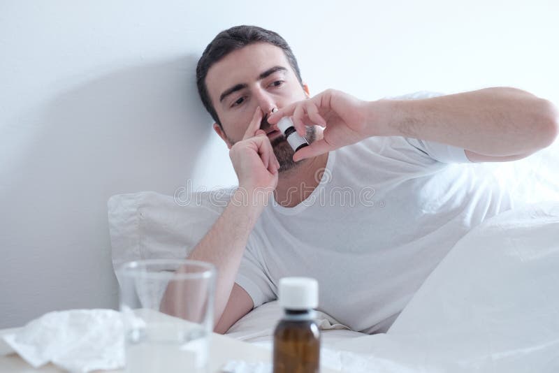 Man Feeling Cold and Using a Nasal Spray Lying in the Bed Stock Photo ...