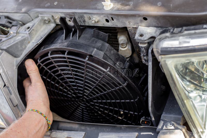A Man Fixes an Engine Cooling Fan Under the Radiator Grill of a Car ...