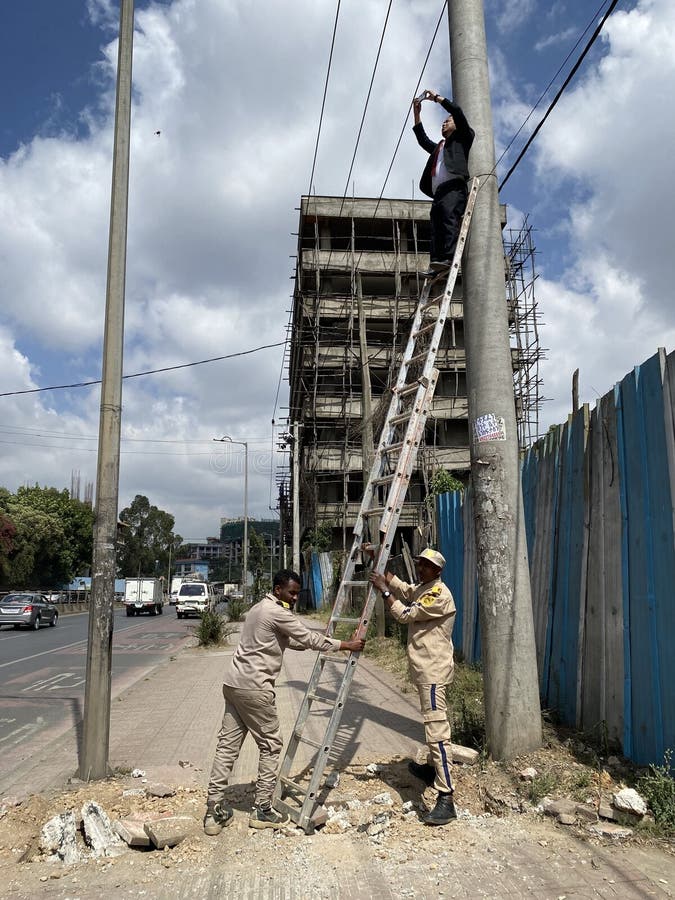 Man is Focused on Taking Photos while Climbing a Ladder Held by Two ...