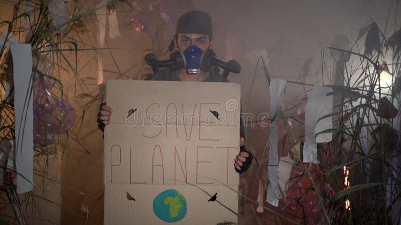 A Man in a Gas Mask Holding Poster with Words Save Planet. Burning ...