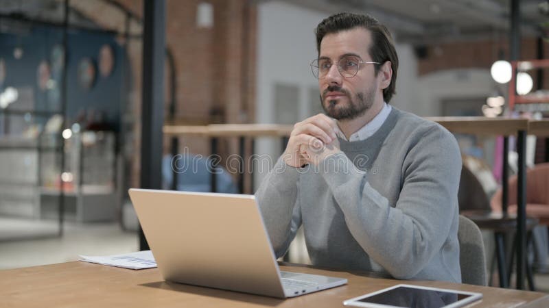 Young Man Thinking while Working on Laptop in Office Stock Photo ...