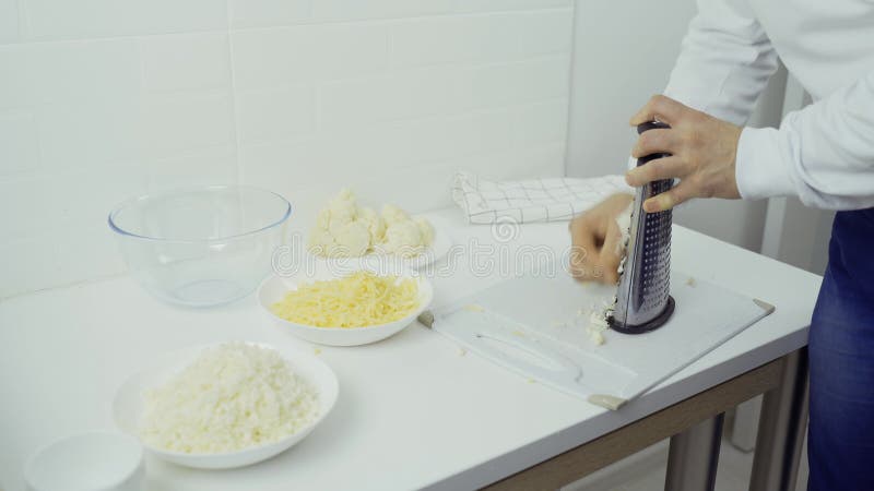 A Man is Grating Cheese; There are Other Ingredients on the Table ...