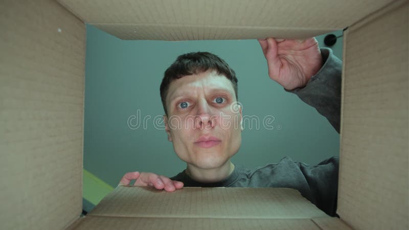 A Man in a Gray Sweater Opens a Cardboard Box, Looks Inside with a ...