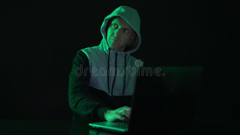 Man is a Guy, a Hacker in the Hood, at the Computer, Looks at the ...