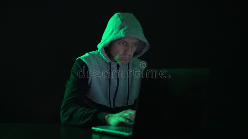 Man a Hacker in the Hood, at the Computer, Looks at the Monitor and ...