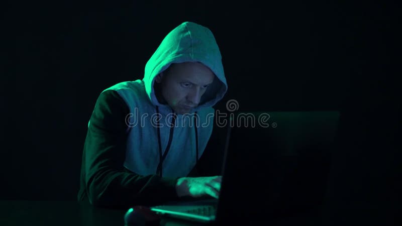 Man a Hacker in the Hood, at the Computer, Looks at the Monitor and ...