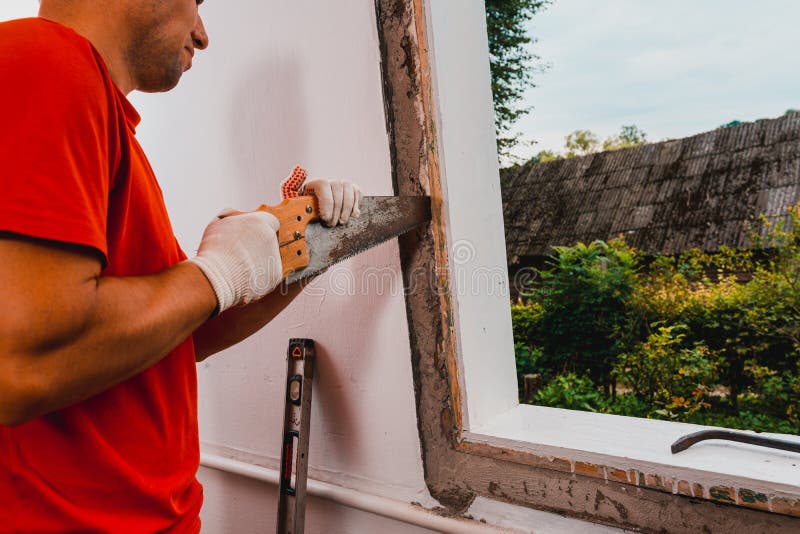 The Man with a Hand Saw Cuts the Mounting Wool Around the Window Frame ...