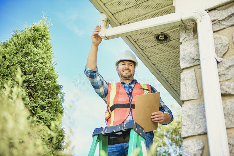 Man with Hard Hat Standing on Steps Inspecting House Gutter Stock Photo ...