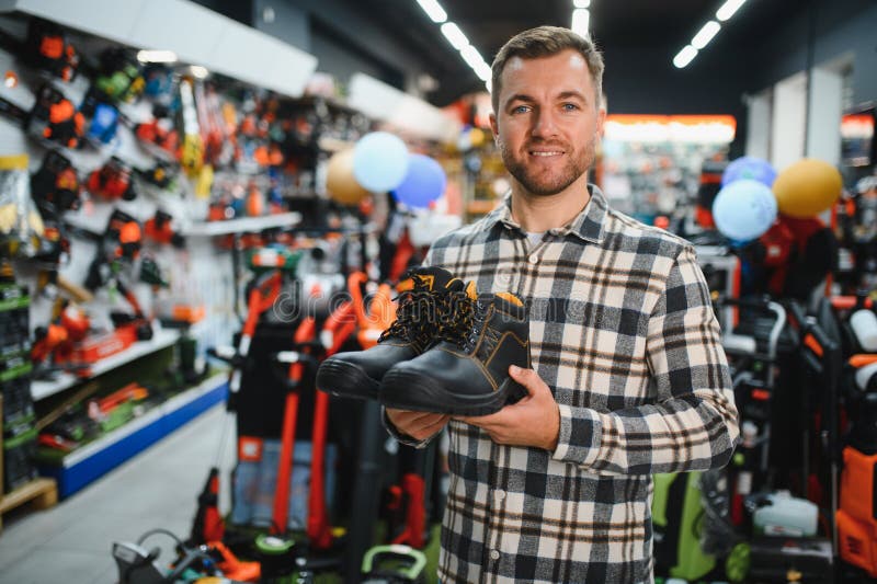 A Man in a Hardware Store Chooses Safety Shoes for Construction Work ...
