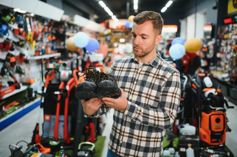 A Man in a Hardware Store Chooses Safety Shoes for Construction Work ...
