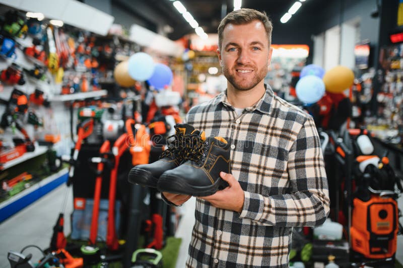 A Man in a Hardware Store Chooses Safety Shoes for Construction Work ...
