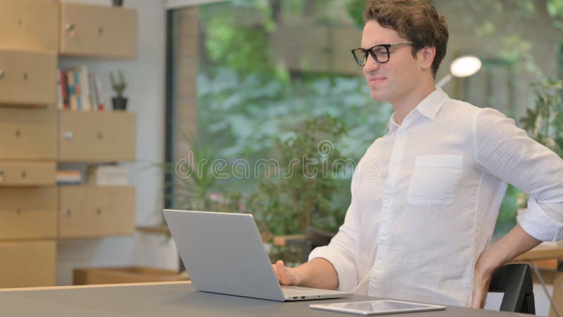 Young Man Having Back Pain while Using Laptop in Modern Office Stock ...