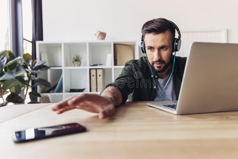 Man in Headphones Using Laptop and Reaching for Smartphone Stock Photo ...