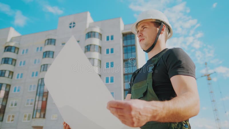 A Man in a Helmet is Holding a Construction Plan in His Hands. a ...