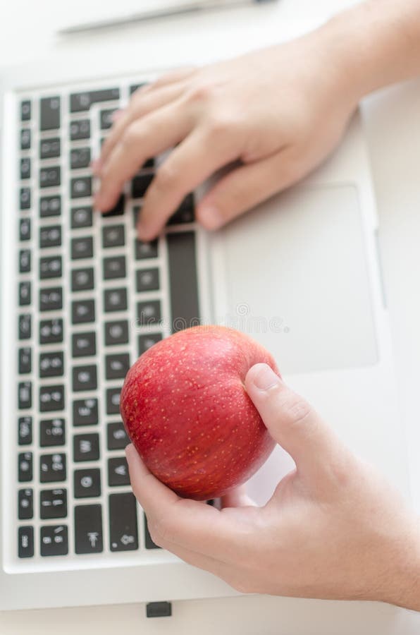 Man Holding an Apple while Typing on His Laptop Stock Image - Image of ...