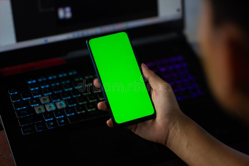 Man Holding Cell Phone with Bright Green Screen in Front of Laptop ...