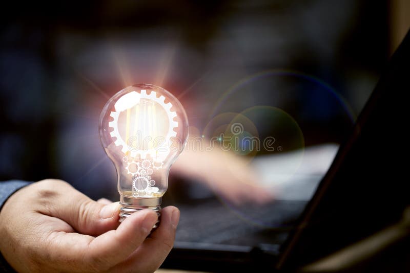 Man Holding a Cog-shaped Light Bulb Inside and Using a Notebook ...