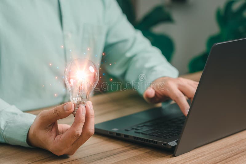 Man Holding a Light Bulb while Working on the Computer To Think and ...