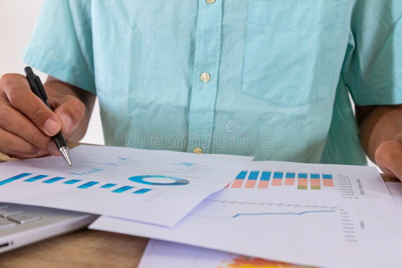 A Man Holding a Pen and Analyzing a Graph of a Report at Workplace ...