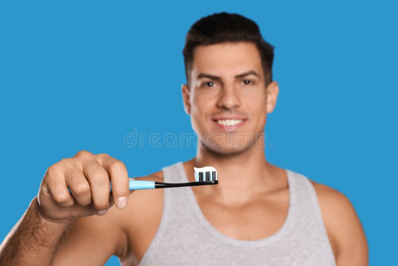 Man Holding Toothbrush with Paste Against Blue Background, Focus on ...