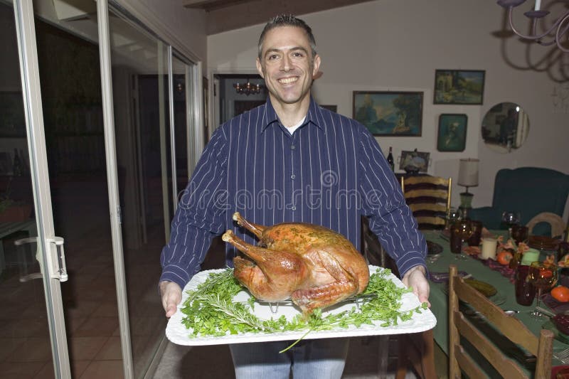Man Holds Cooked Turkey in Front of a Table Set for Thanksgiving Dinner ...