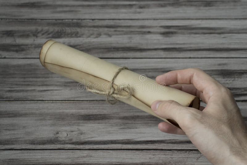 Man Holds in His Hand an Ancient Rough Scroll Against a Wooden Surface ...