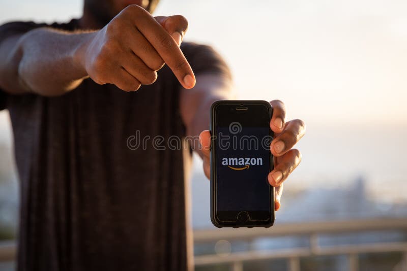 A Man Holds a Smartphone with the Amazon Logo. is an American ...