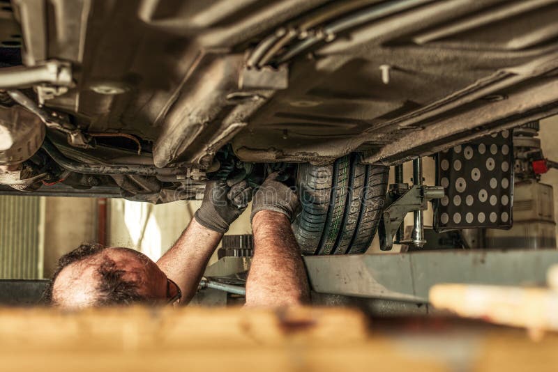 Man in a Hole Under a Car Fixing Steering Alignment in a Garage Stock ...