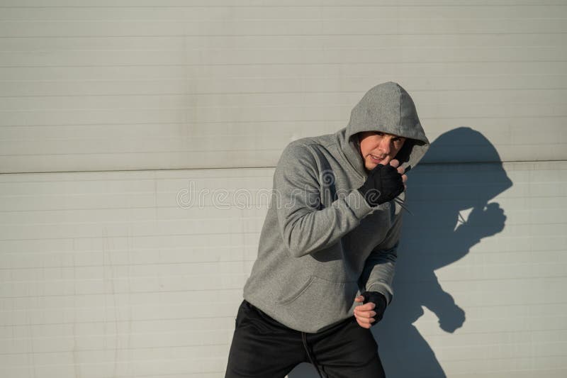 A Man in a Hoody Trains Boxing Against a Gray Wall. Stock Photo - Image ...