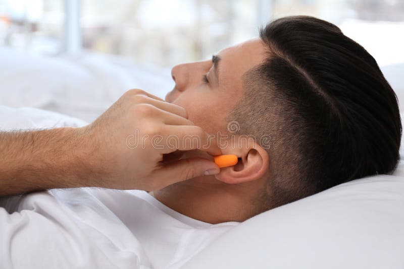 Man Inserting Foam Ear Plugs in Bed, Closeup Stock Photo - Image of ...