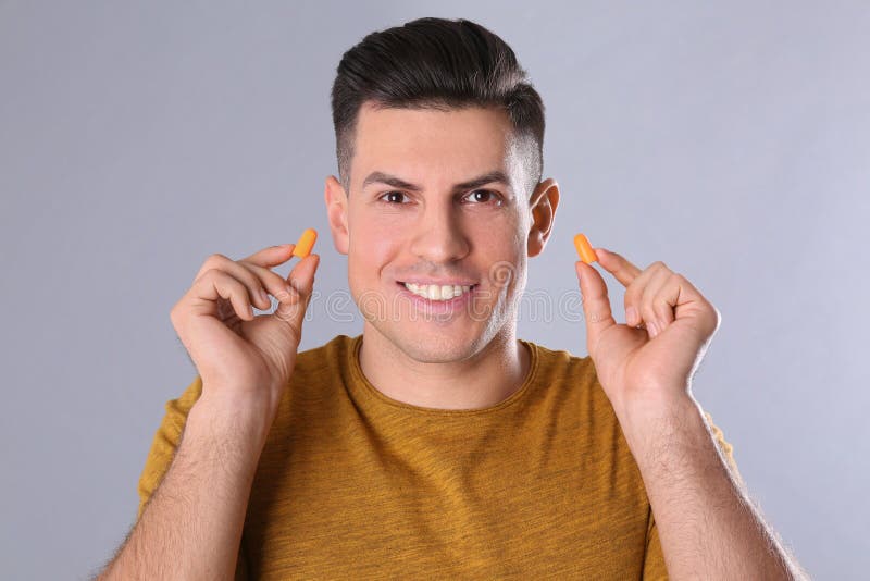 Man Inserting Foam Ear Plugs on Grey Background Stock Photo - Image of ...