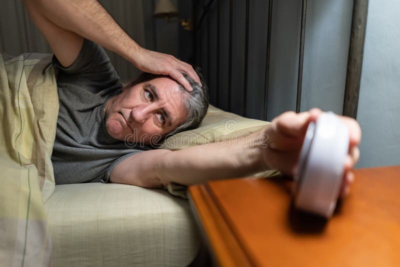 Man with Insomnia Lying in Bed and Looking at the Time on the Clock ...