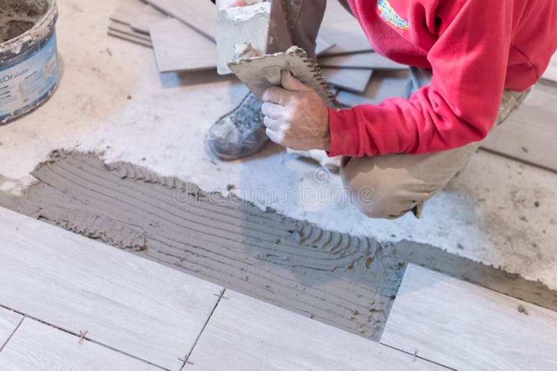 Man Installing Rectangular Shaped Floor Tiles in Kitchen. Applying Adhesive before Installation ...