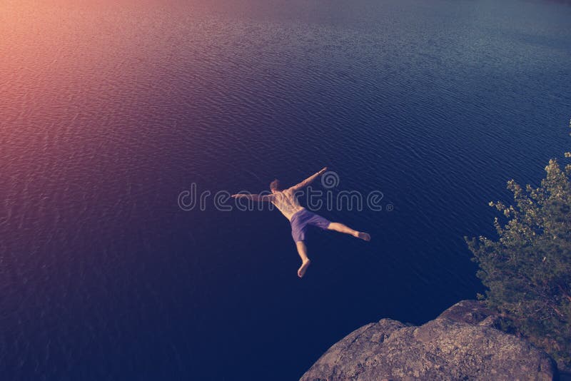 Man Jumping into the Water from Cliff at Sunset with Outspread Hands ...