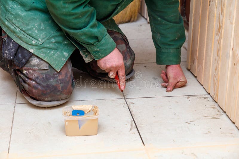A Man is Kneeling on the Floor and Cutting Something with a Pair of ...