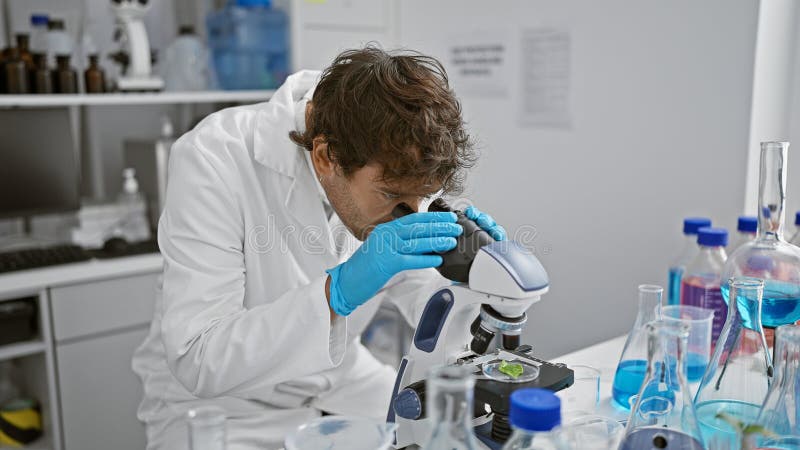 A Man in a Lab Coat Examines a Specimen Under a Microscope in a Well ...