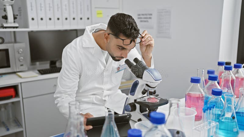 A Man in a Lab Examines Samples through a Microscope Surrounded by Test ...
