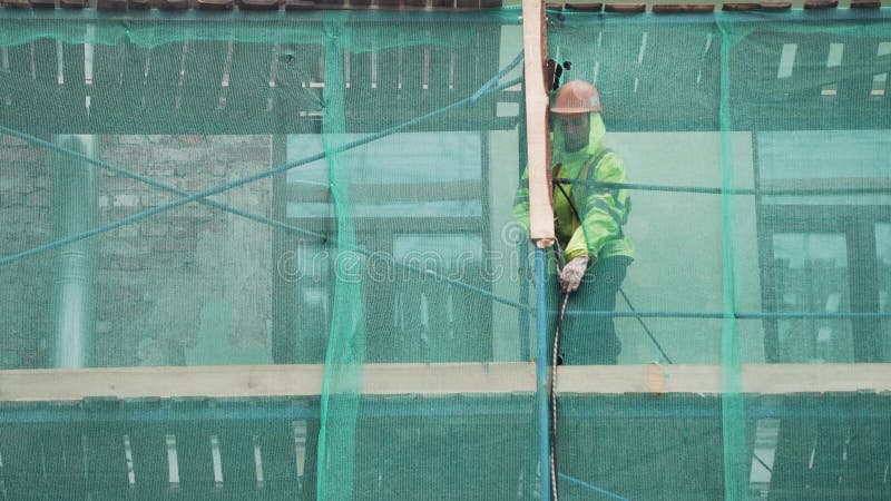 Male Laborer Wearing Uniform Pulls Up Rope on Scaffolding Covered by ...