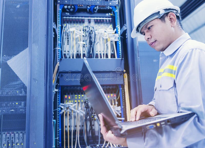 A Man with a Laptop Sits in the Server Room of the Data Center. the ...