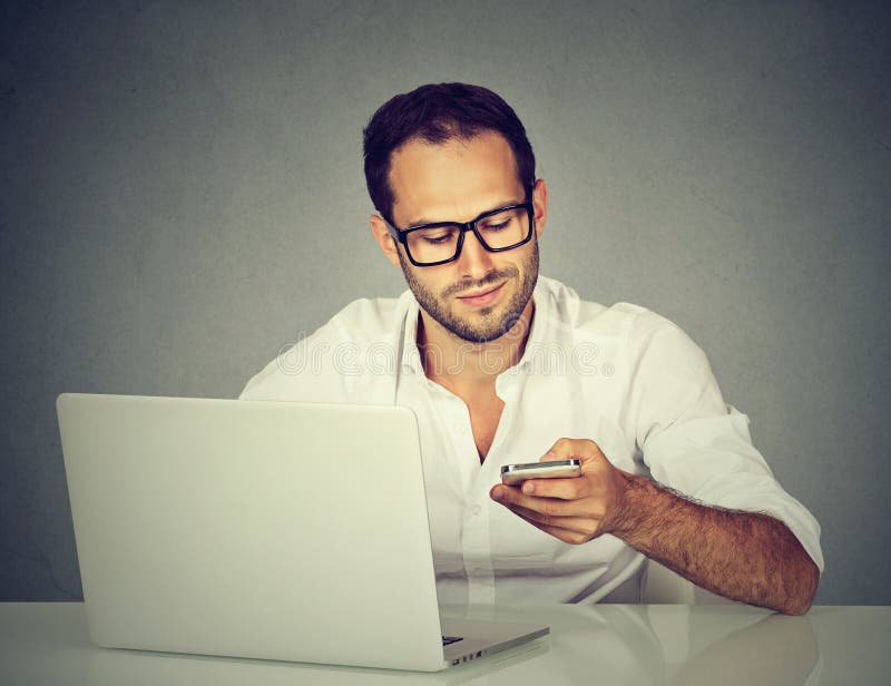 Man with Laptop Texting on Mobile Phone Sitting at Table Stock Photo ...