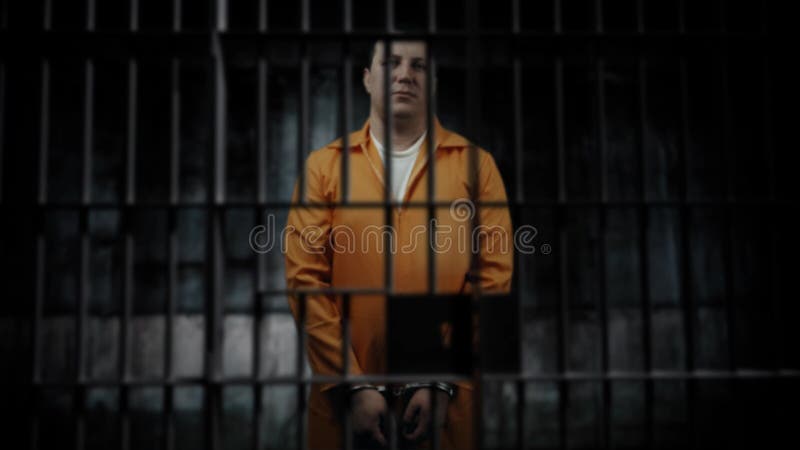 A Man is Locked in a Prison Cell. Prisoner with Handcuff is Looking at ...