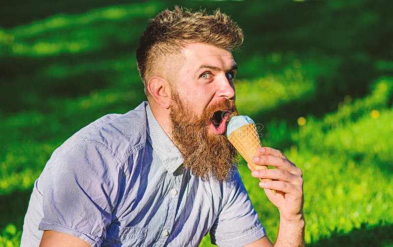 Man With Long Beard Enjoy Ice Cream While Sits On Grass Bearded Man