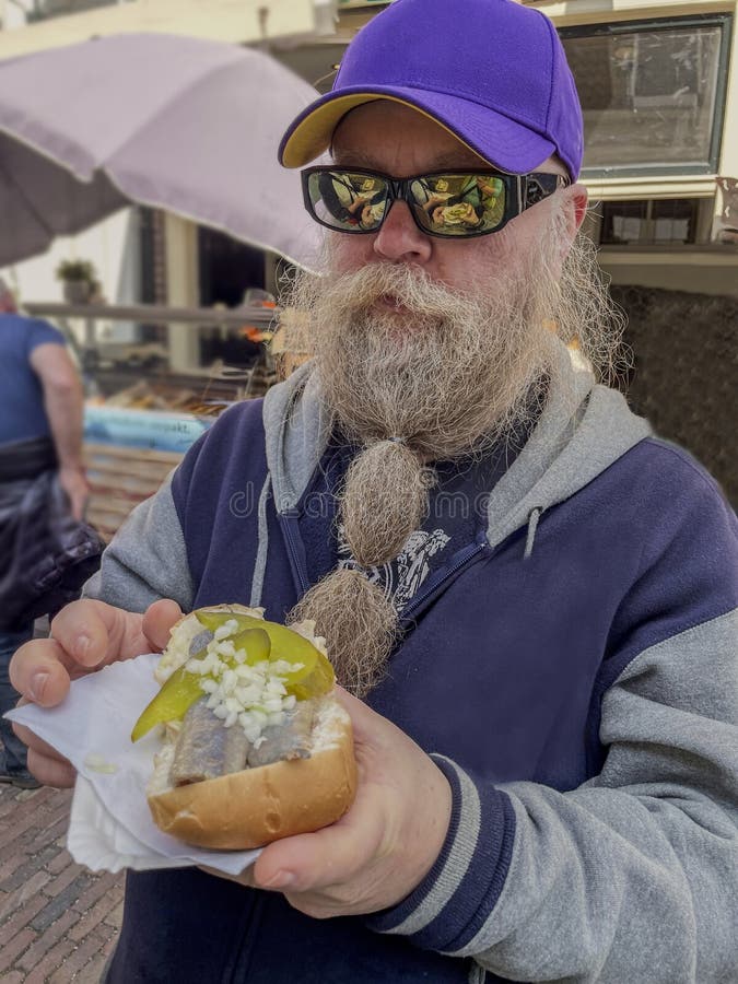 Man with Long Beard, Glasses and Cap, Sits Thoughtfully by a Wall Stock ...