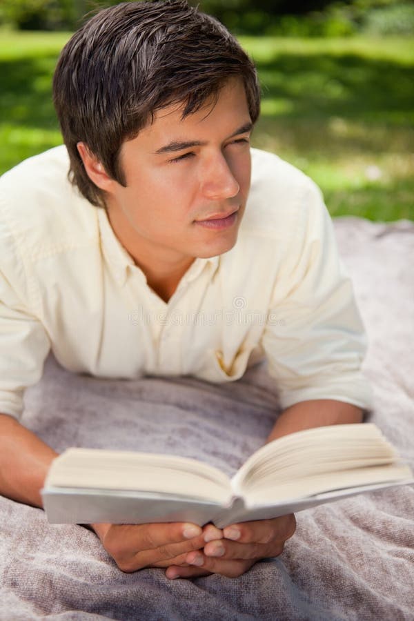Man Looking To His Side while Reading a Book As he Lies on a Blanket ...