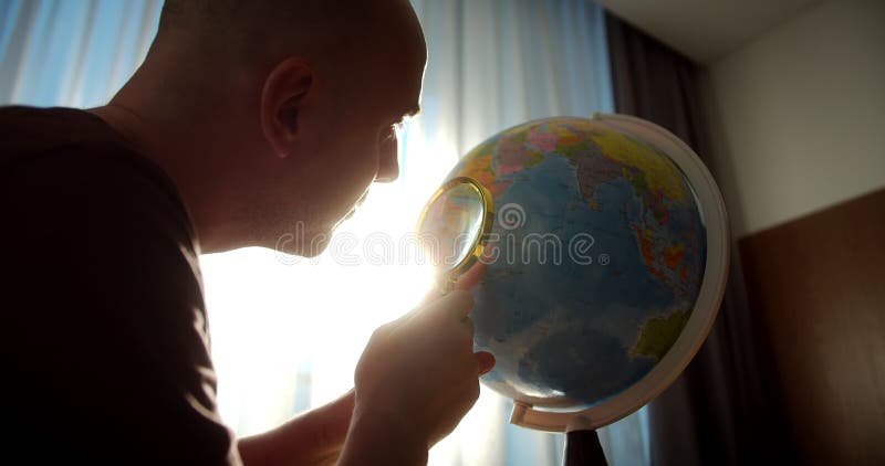 Man Looks through a Magnifying Glass at a Globe. Man Using Globe Sits ...