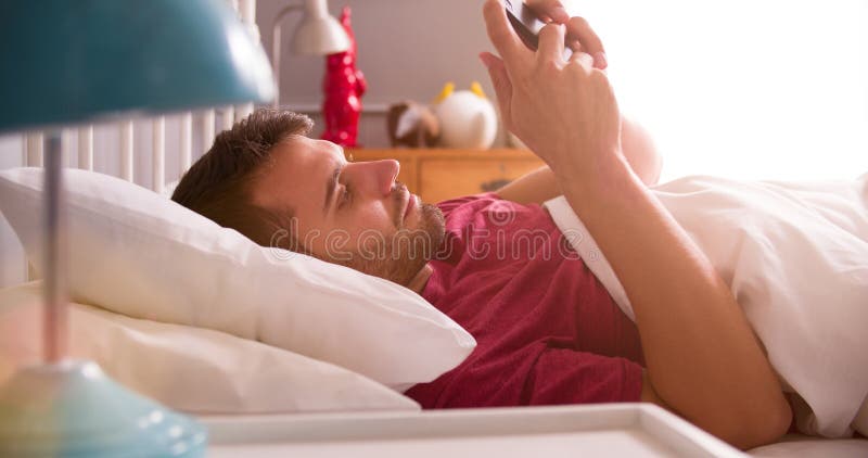 Man Lying in Bed Checking Messages on Mobile Phone Stock Photo - Image ...