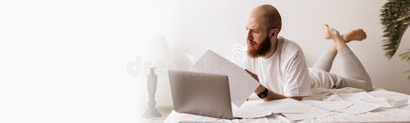 Man Working with Paper Documents Using Laptop while Lying in Bed Stock ...