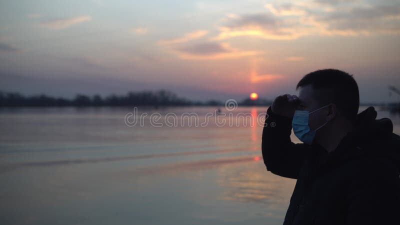 A Man in a Mask Stands by the River, Lake and Looks at the Sunset Stock ...