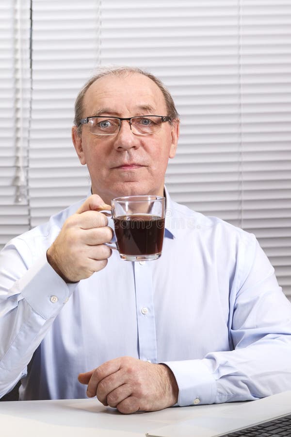 A Man in the Office with Glasses at the Computer Drinks Coffee Stock ...