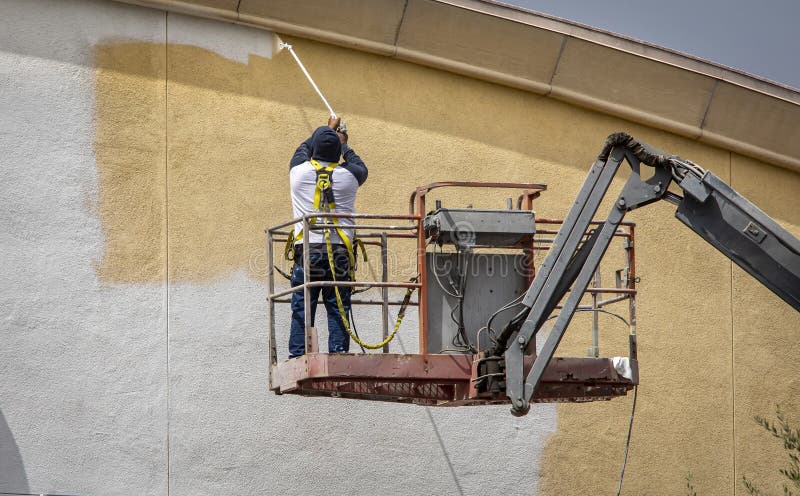 Man Painting a Yellow Wall White Using a Paint Sprayer while Standing ...